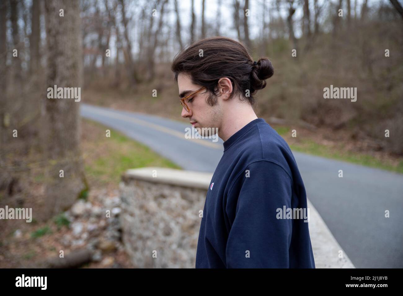 Side view of young man alone outdoors looking down in contemplation ...