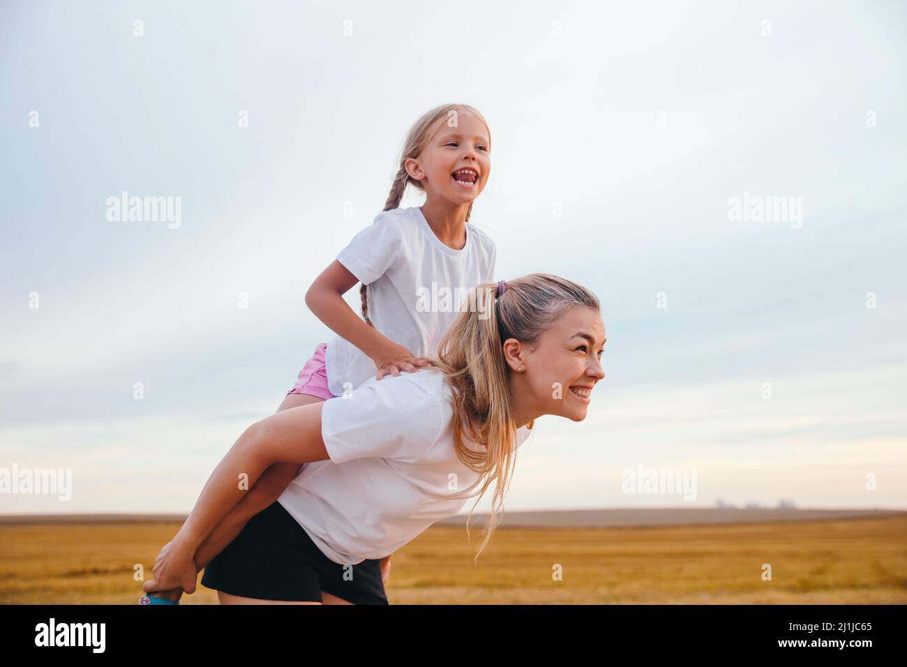 Portrait of young mother carrying her daughter on her back. Happy ...