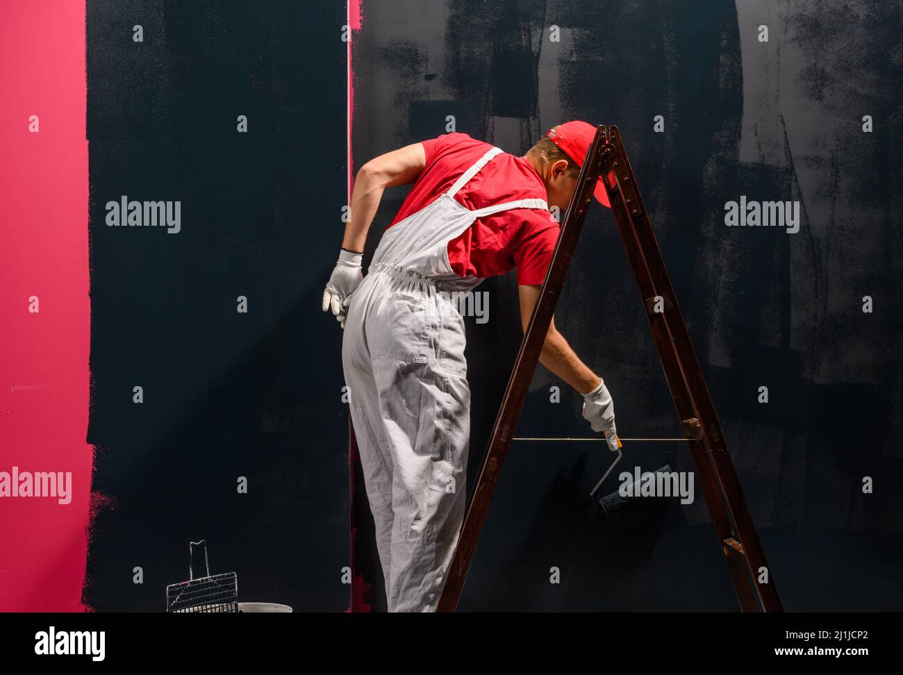 Man painting a wall. Painter in red overall painting wall in black ...