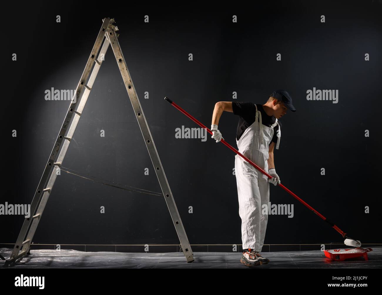 Man painting a wall. Painter in red overall painting wall in black ...