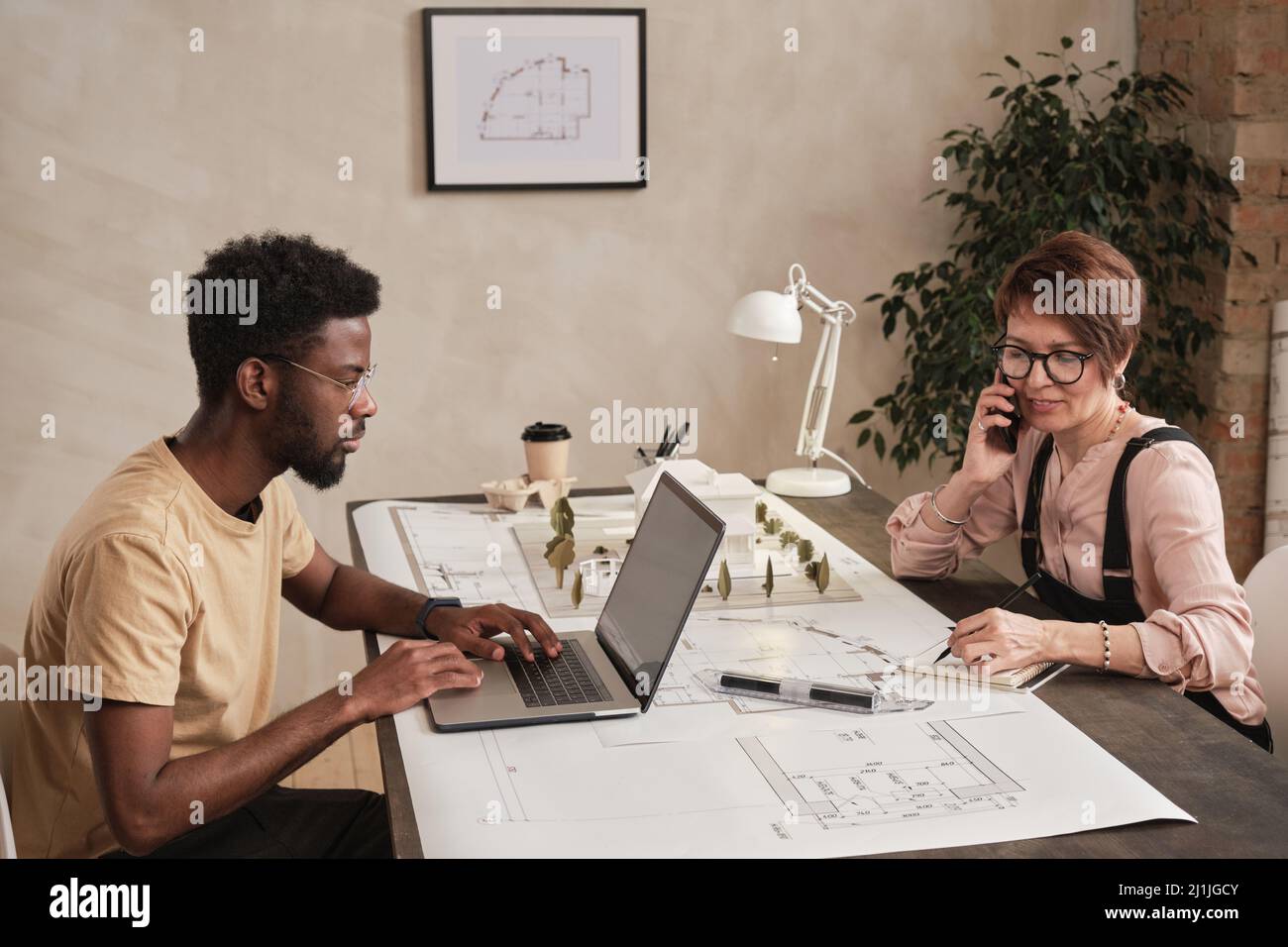 Busy multi-ethnic employees sitting at table and working with devices in modern work space of ...