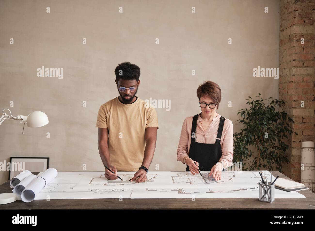 Concentrated multi-ethnic architects in glasses standing at table in ...