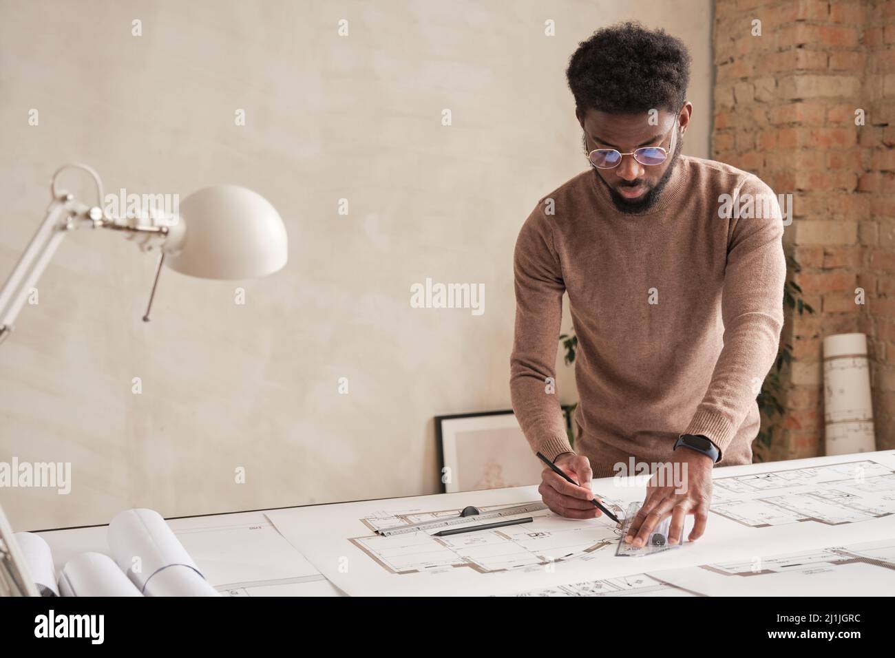 Serious young Black man in brown turtleneck and glasses standing at ...