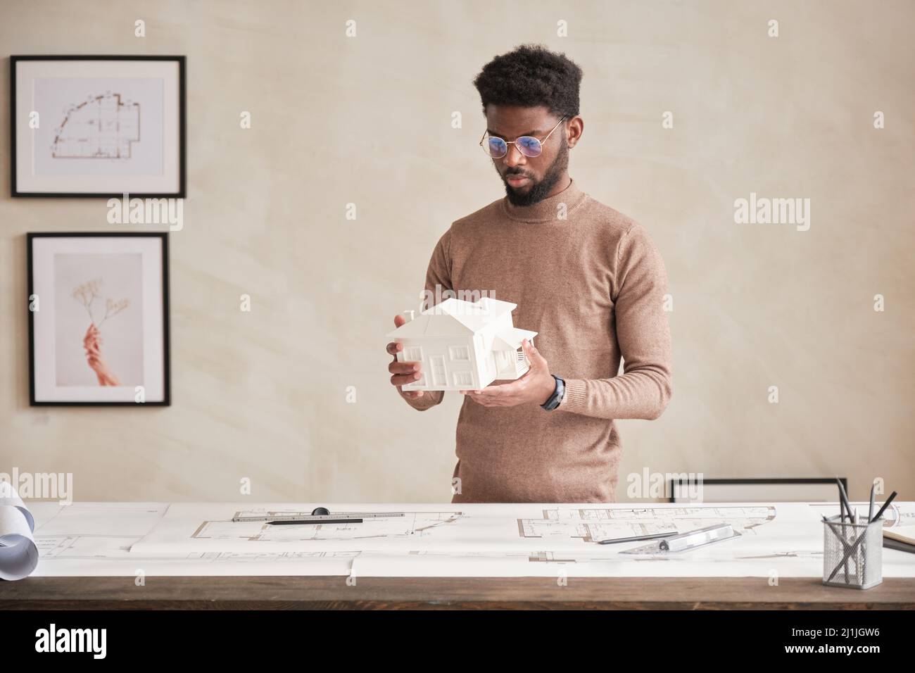 Serious young black architect with beard standing at table with floor ...