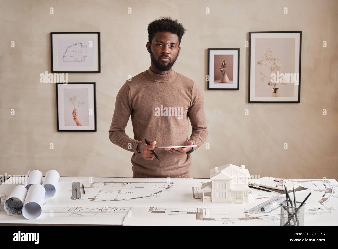 Portrait of serious young bearded black architect in sweater standing ...