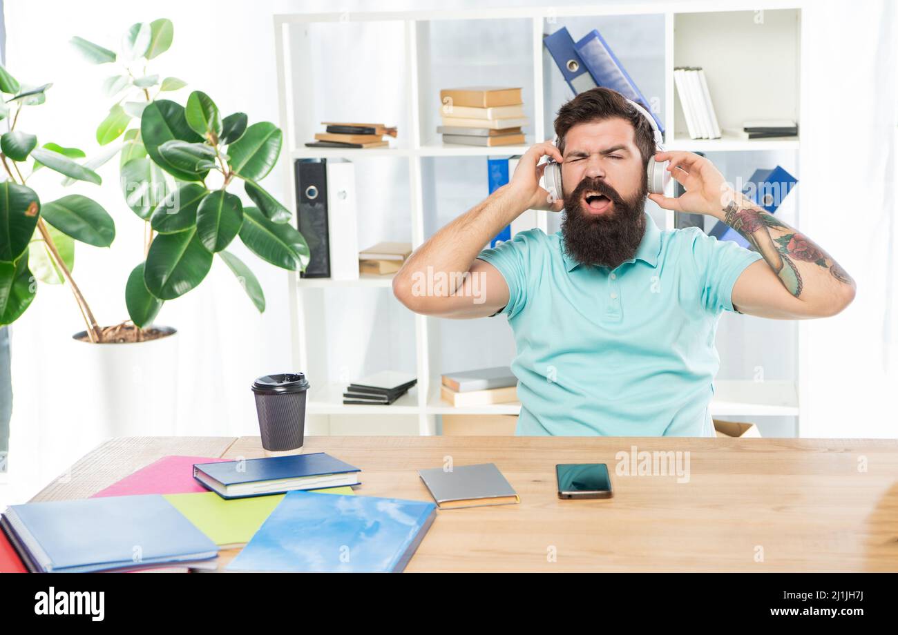 Happy man singing along while listening to song in headphones in office ...