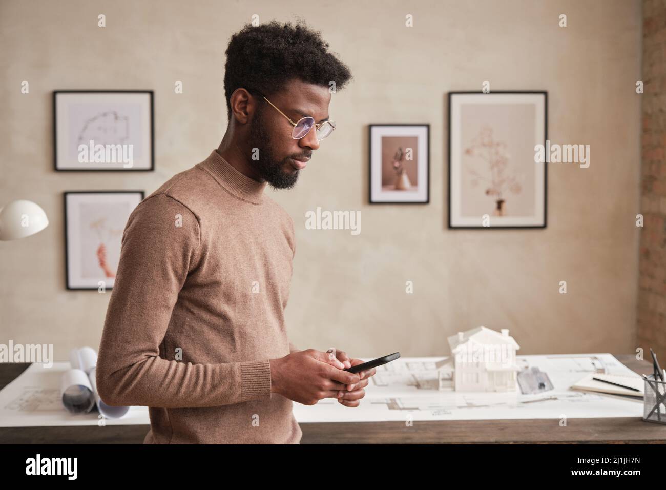 Busy young African-American architect with beard standing against table ...
