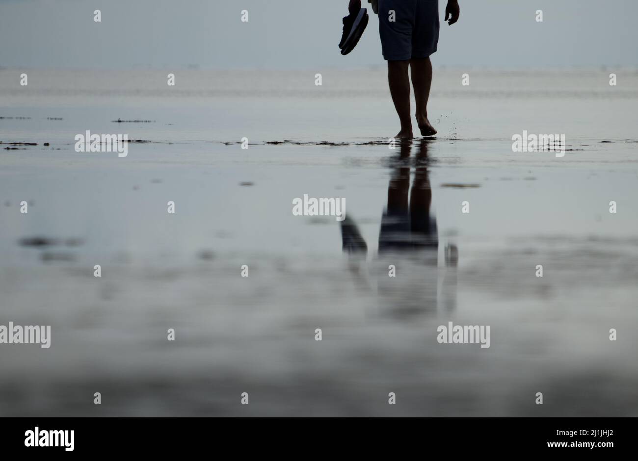 Man carrying shoes walking on the surface of low tide sea coastline ...