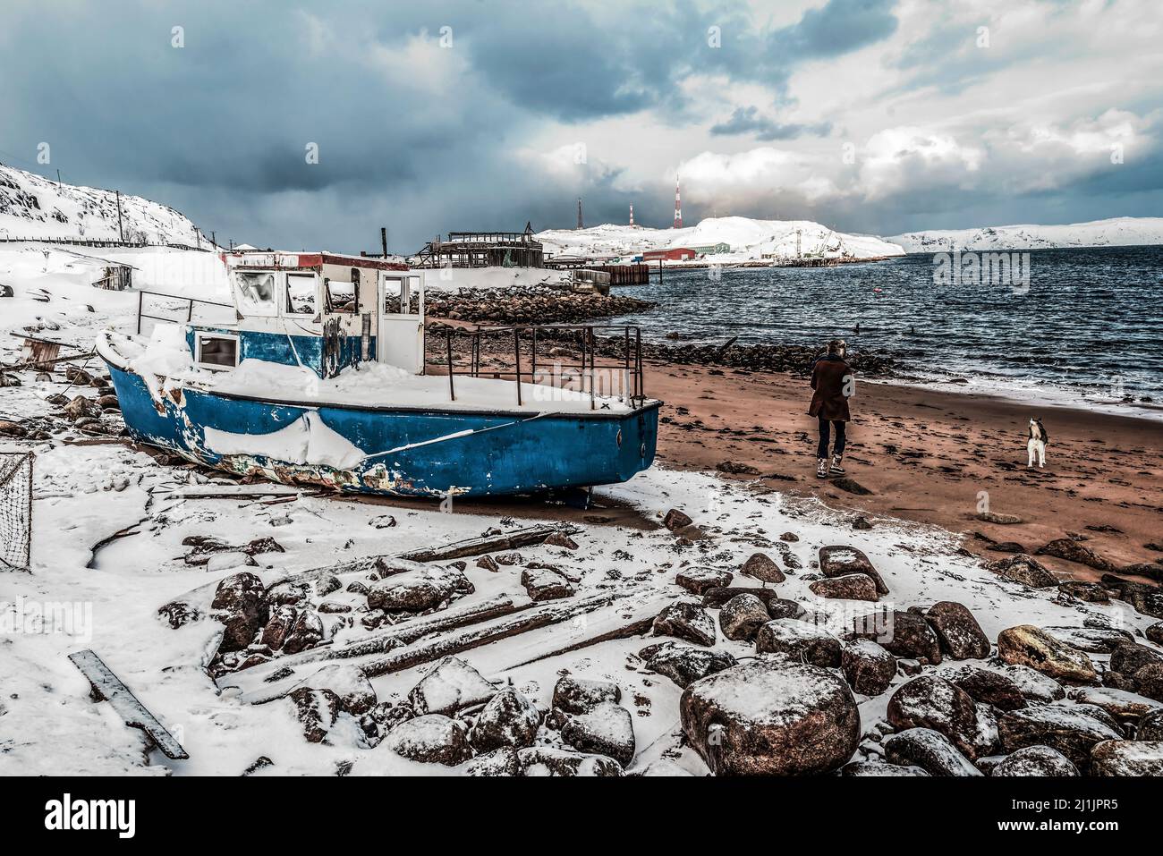 Man with a dog walking near an old ship moored by the sea in Teriberka ...
