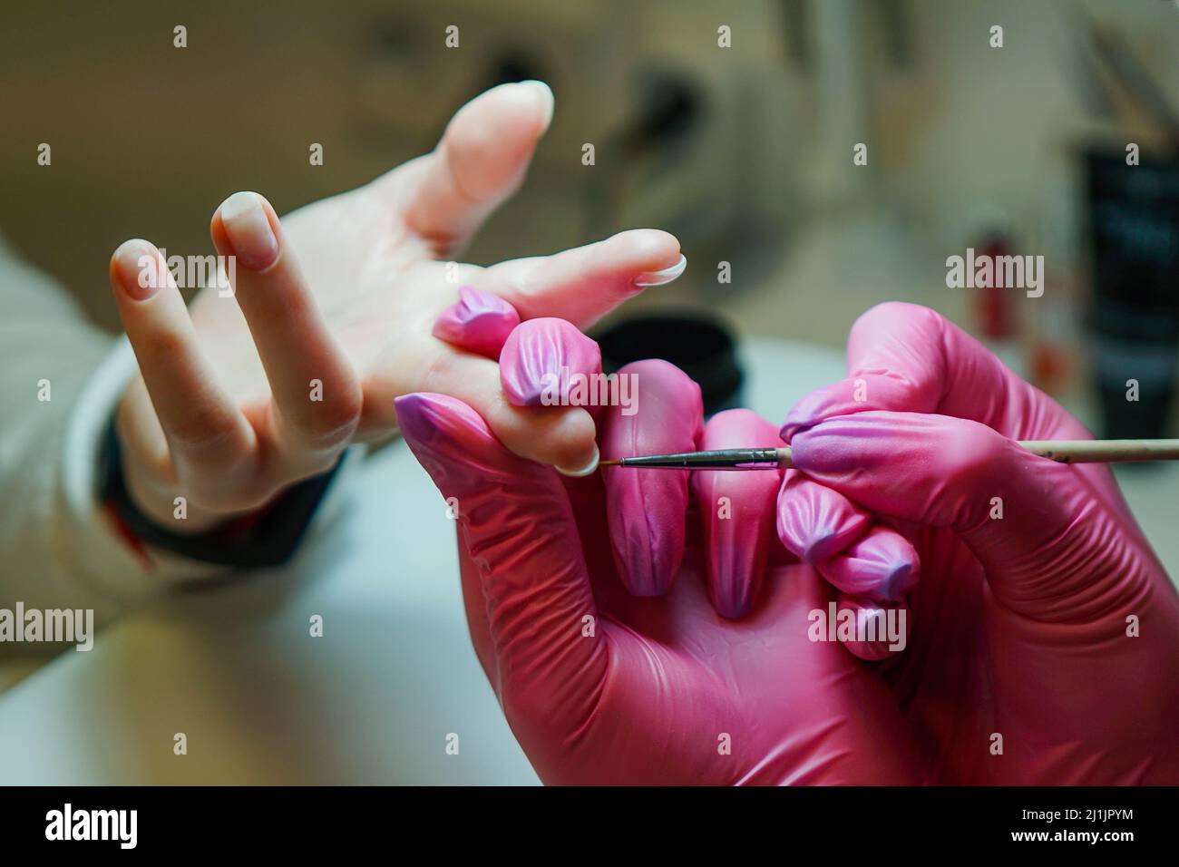 Close up of manicure master in rubber gloves applying red nails in the ...