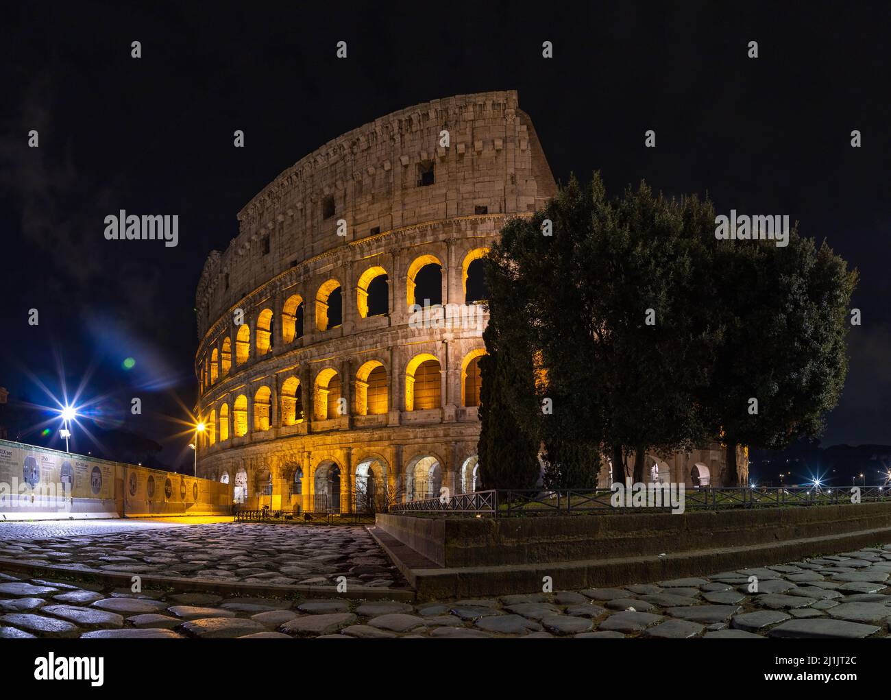 A picture of the Colosseum at night, partially hidden by some trees ...