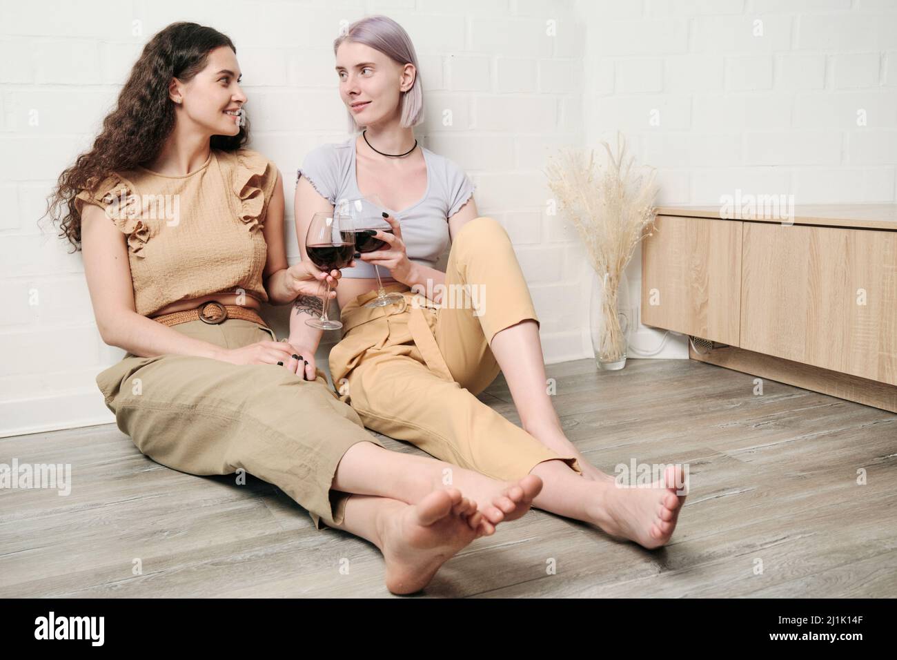 Happy Young Caucasian Lesbians Sitting On Floor And Clinking