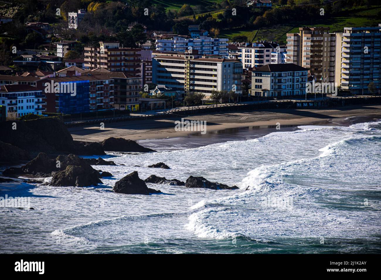 An aerial view of the sea waves splashing on the beach of small coastal ...
