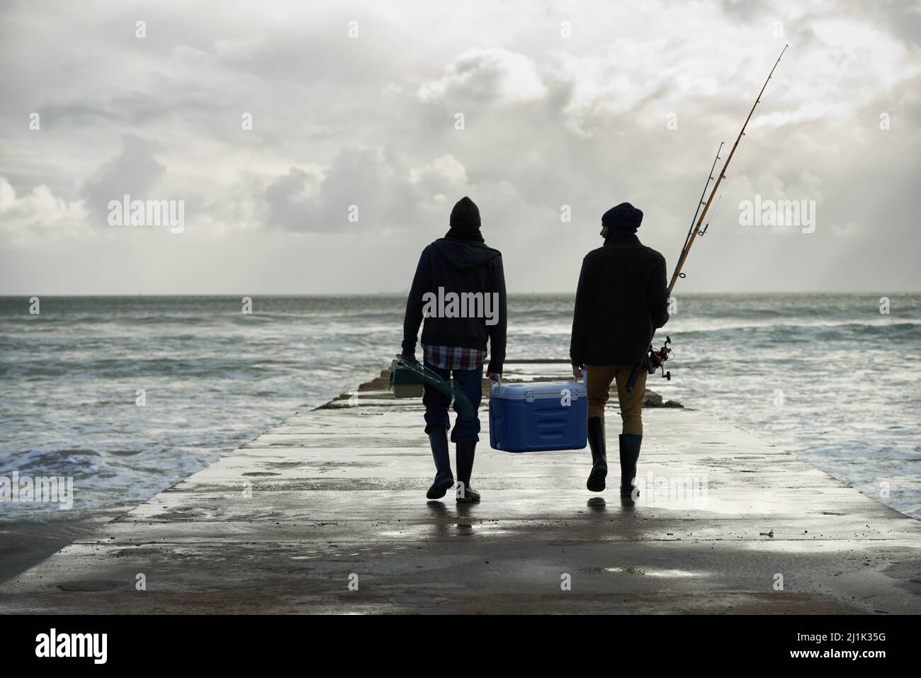 Carrying home their catch. Shot of two young men fishing at the ocean ...