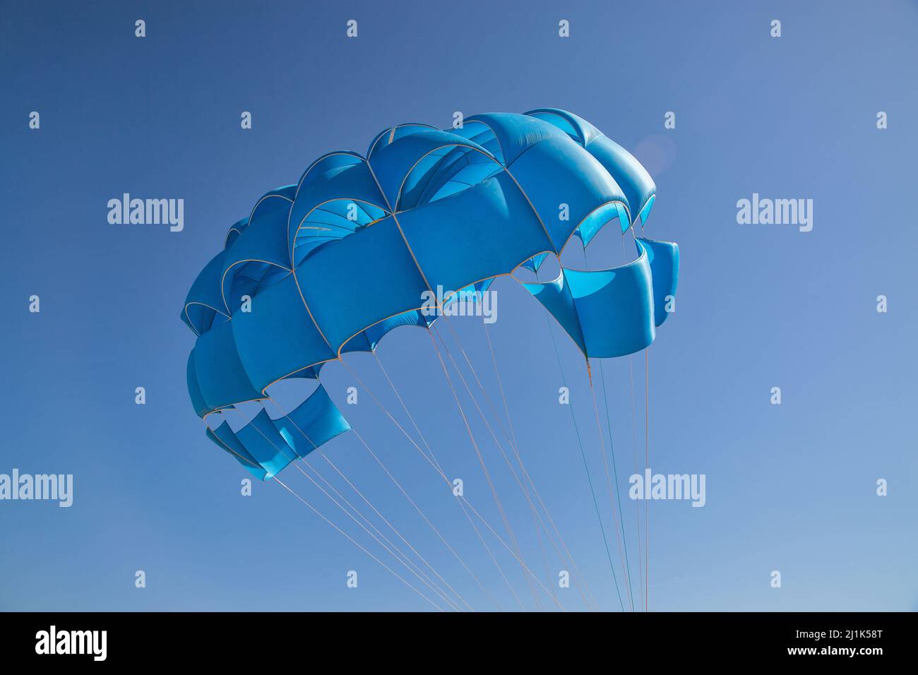 Blue open parachute for paragliding watersports against clear blue sky ...