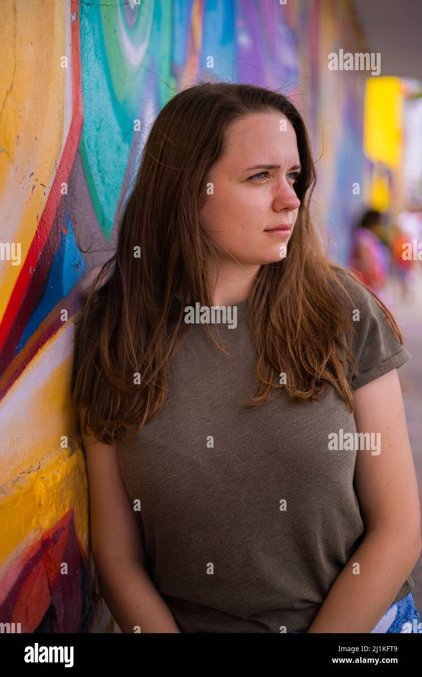 Young and beautiful woman leans against a colorful wall and poses for ...