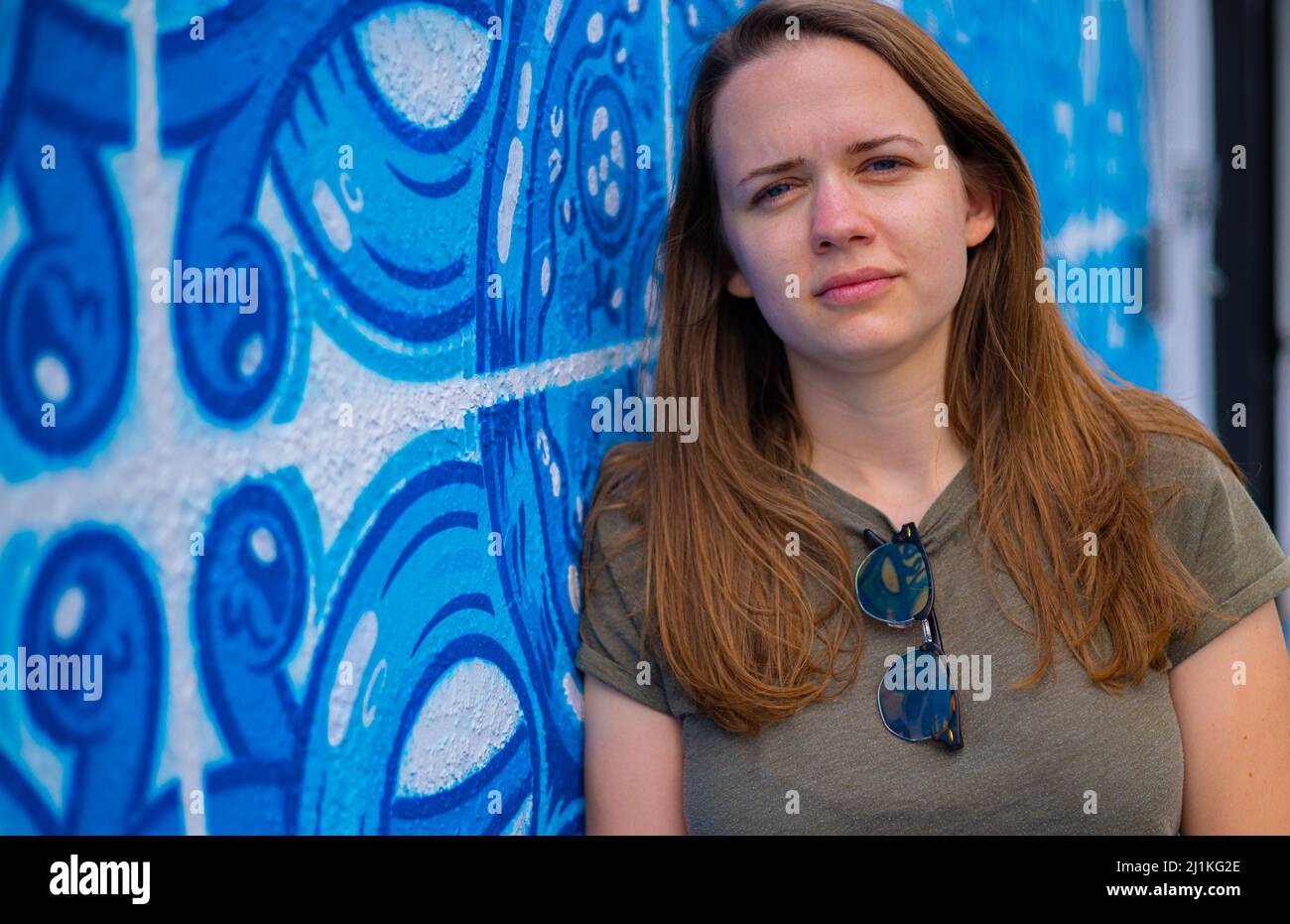 Young and beautiful woman leans against a colorful wall and poses for ...
