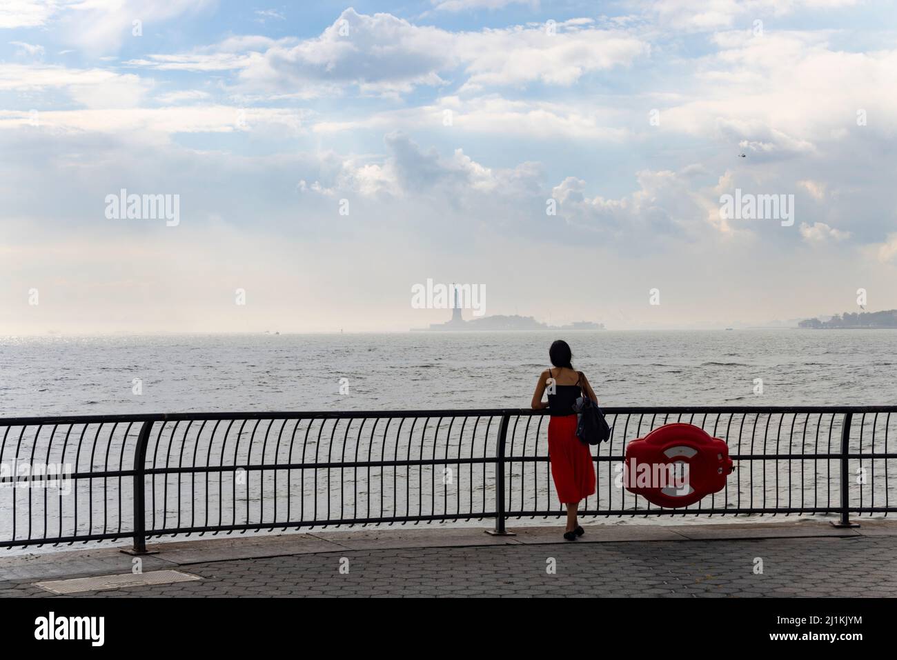 A woman stands and views the Statue of Liberty at Battery Park NYC ...