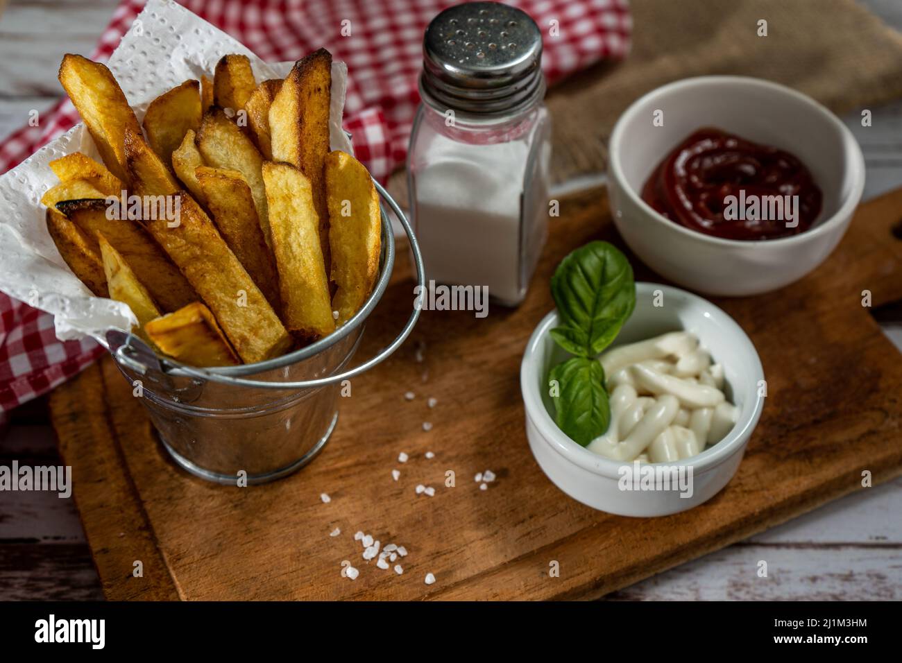 French fries in a metal pot with aioli and ketchup on a wooden board ...