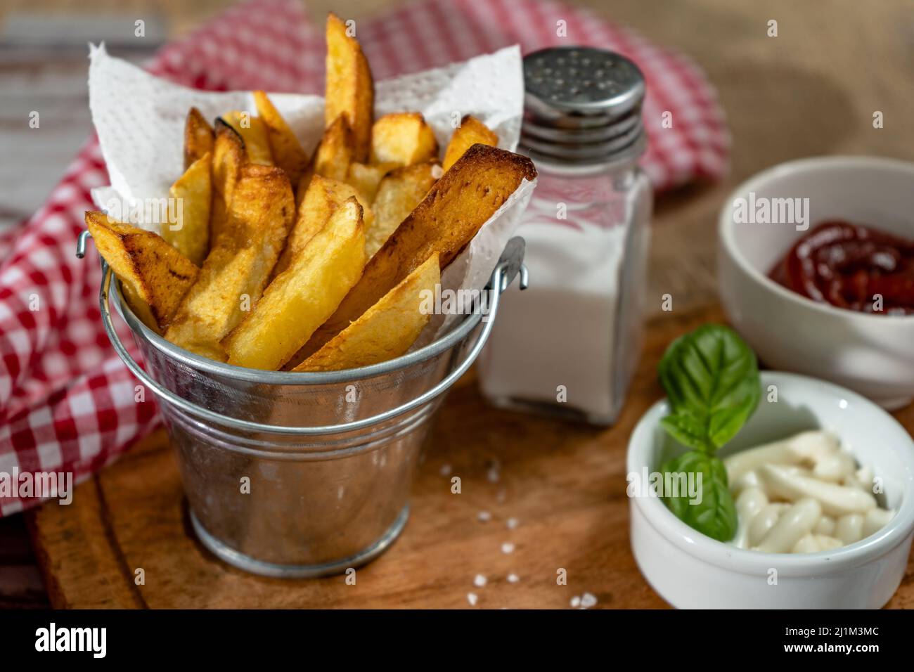 French fries in a metal pot with aioli and ketchup on a wooden board ...