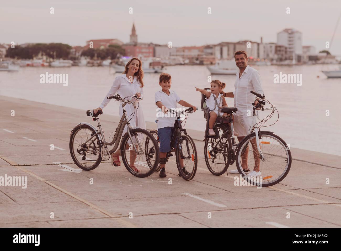 The happy family enjoys a beautiful morning by the sea riding a bike ...