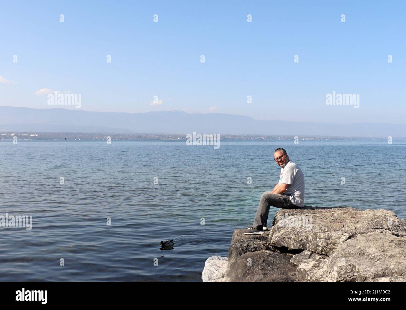 A charming man about 40 years old, sitting on rocks staring out to the ...