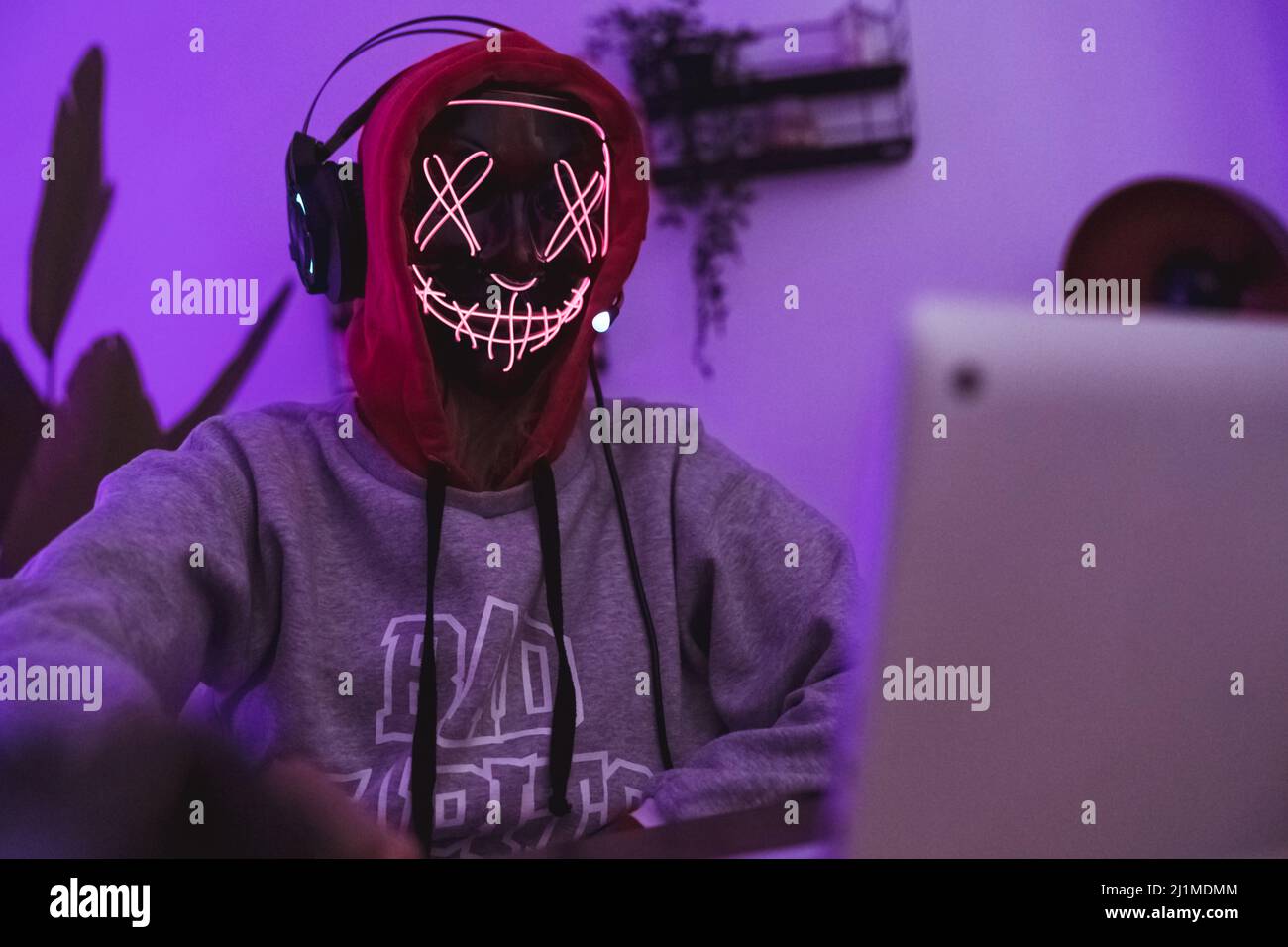 Professional hacker in a scary mask and red hood committing a crime ...