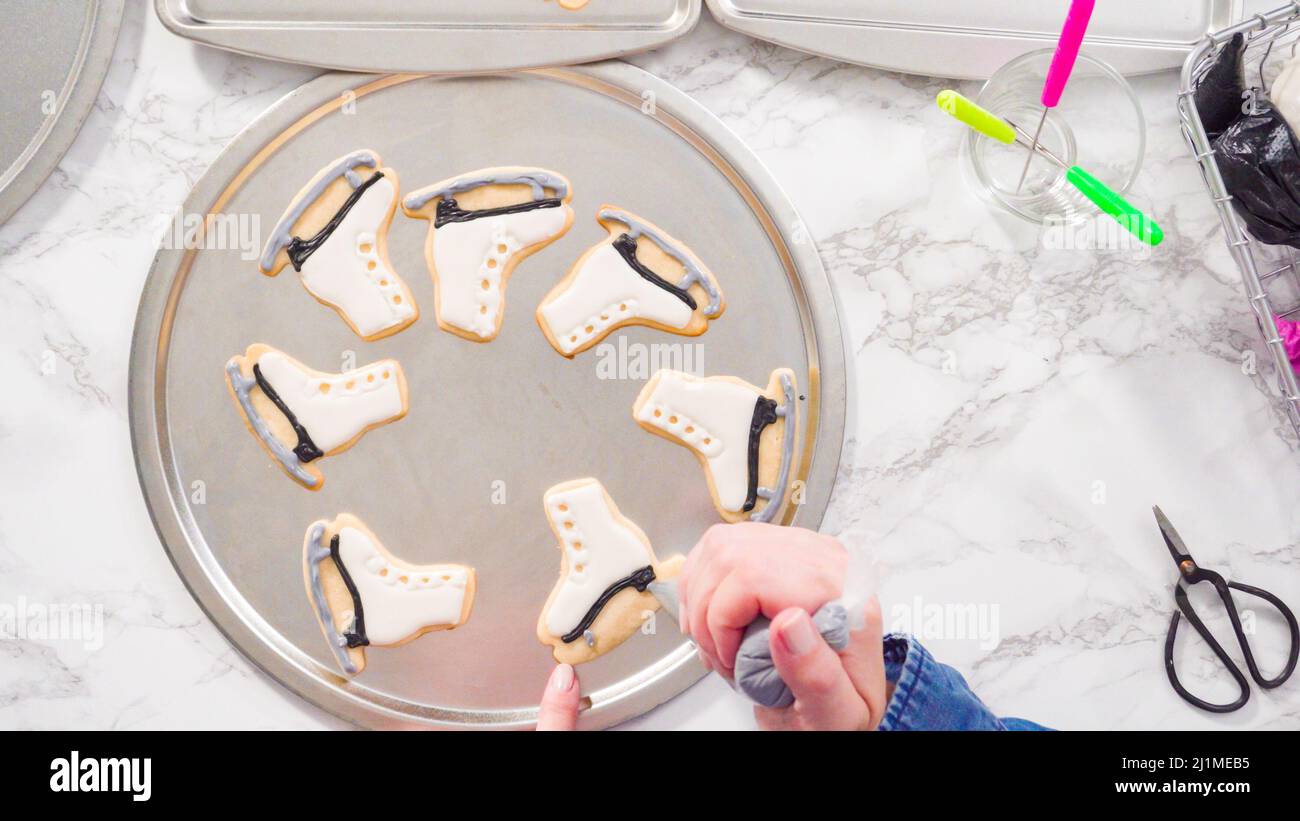 Flat lay. Decorating ice skate shaped sugar cookies with black color ...