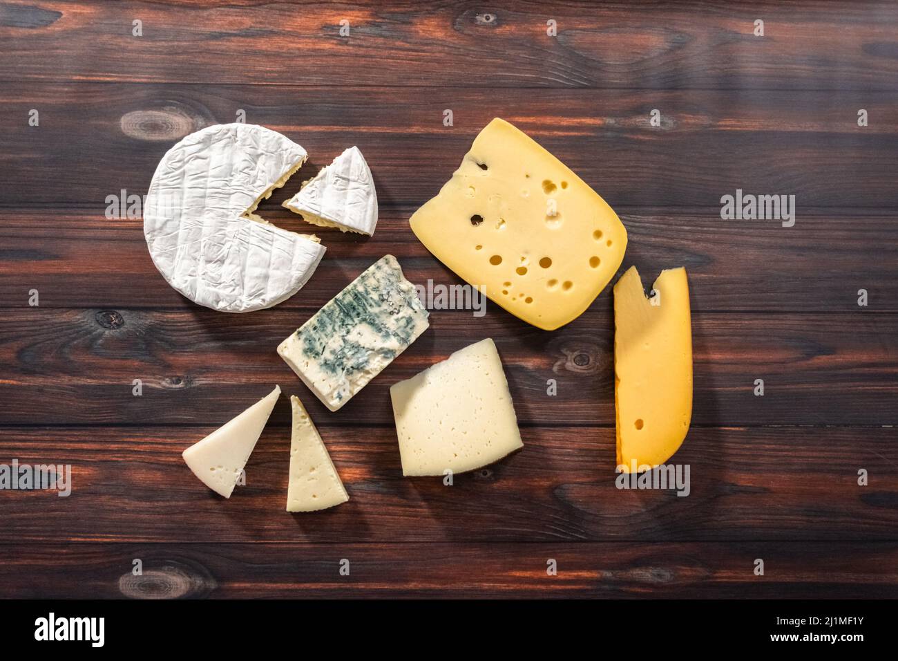 Flat lay. Variety of large gourmet cheese wedges on a dark wooden ...