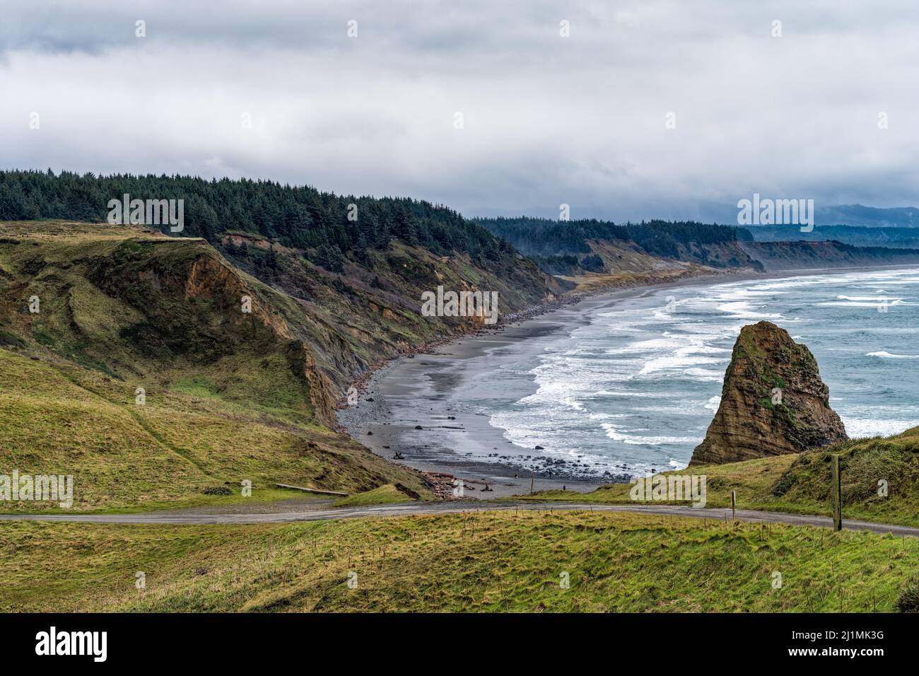 A winding road passes a sea stack on the beach at Cape Blanco State ...