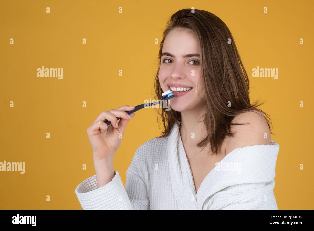Young cheerful woman brushing teeth with toothbrush during morning hygiene procedures isolated ...