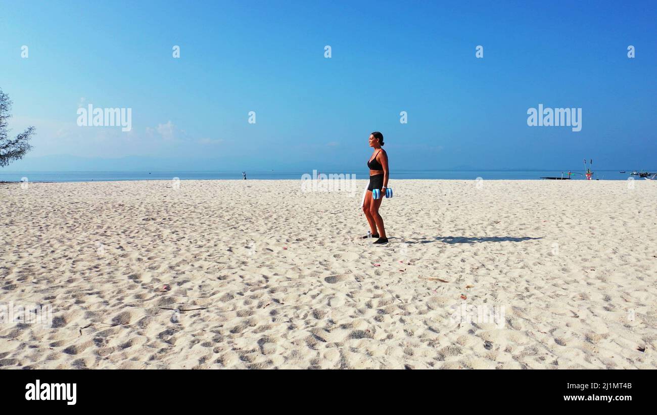 A Caucasian pretty female in a gym outfit exercises with dumbles on the ...