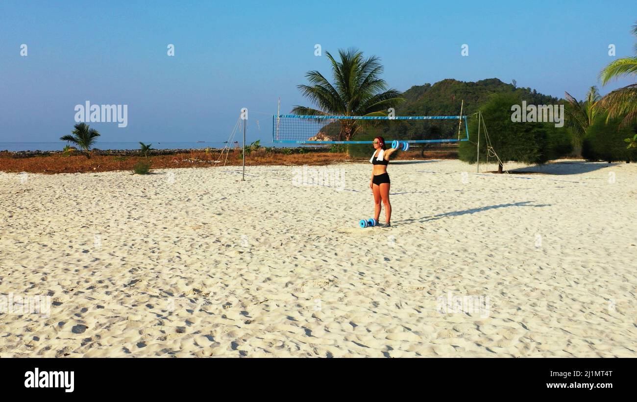 A Caucasian pretty female in a gym outfit exercises with dumbles on the ...