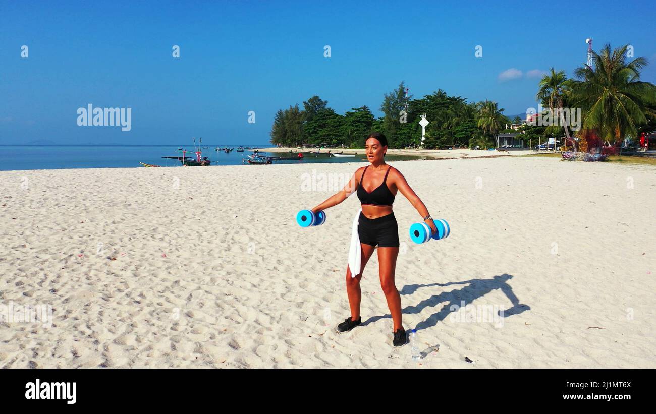 A Caucasian pretty female in a gym outfit exercises with dumbles on the ...