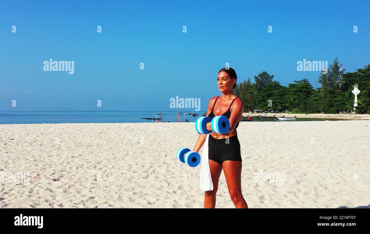 A Caucasian pretty female in a gym outfit exercises with dumbles on the ...