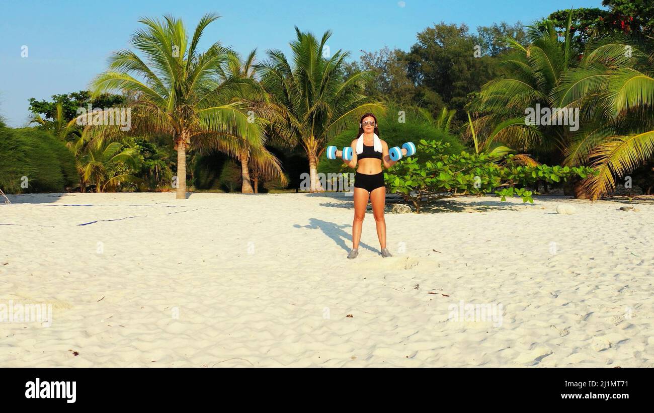 A Caucasian pretty female in gym outfit exercise on the sandy beach, Koh Samui, Thailand with ...