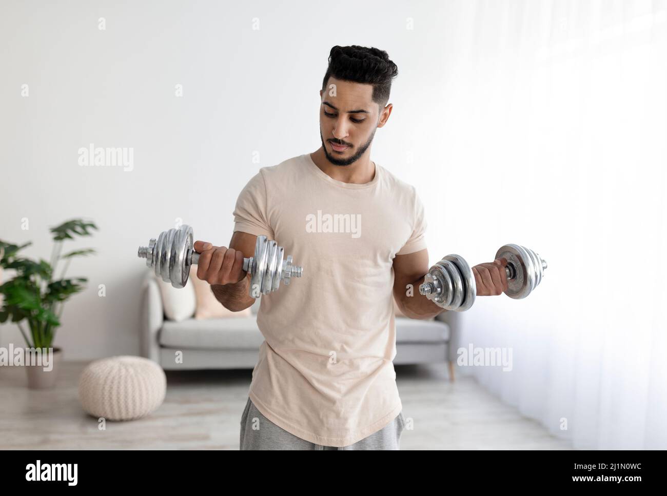 Strong young Arab man exercising with dumbbells at home. Domestic ...