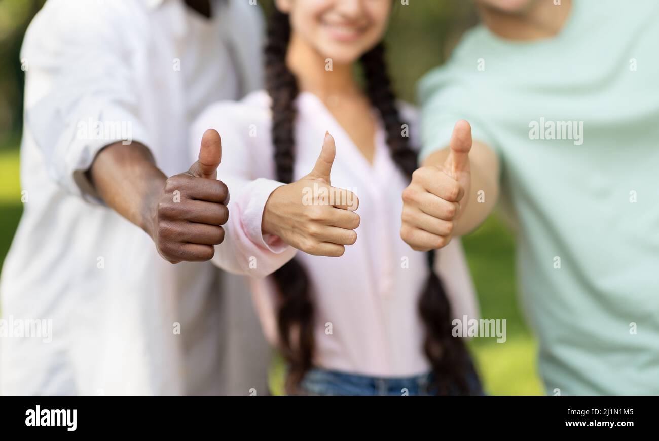 Mixed students gesturing thumbs up, posing outdoors in university ...