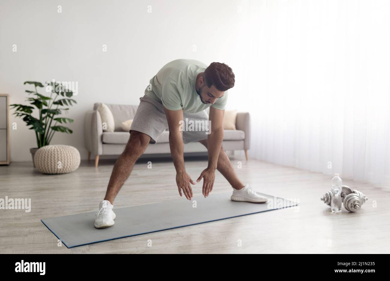 Fit young Arab man doing exercises, stretching legs muscles at home ...
