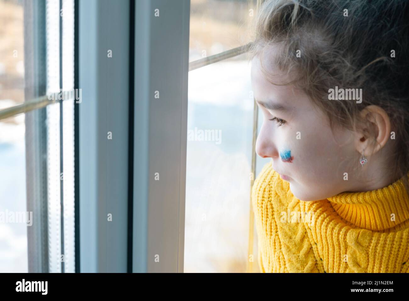 A sad child at the window with the flag of Russia, worries with tears ...