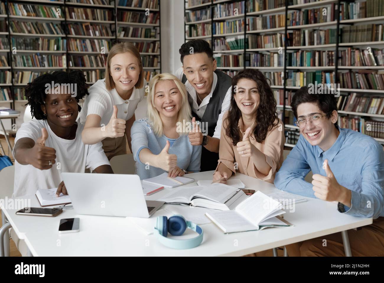 Multiracial students gather in library showing thumbs up at camera ...