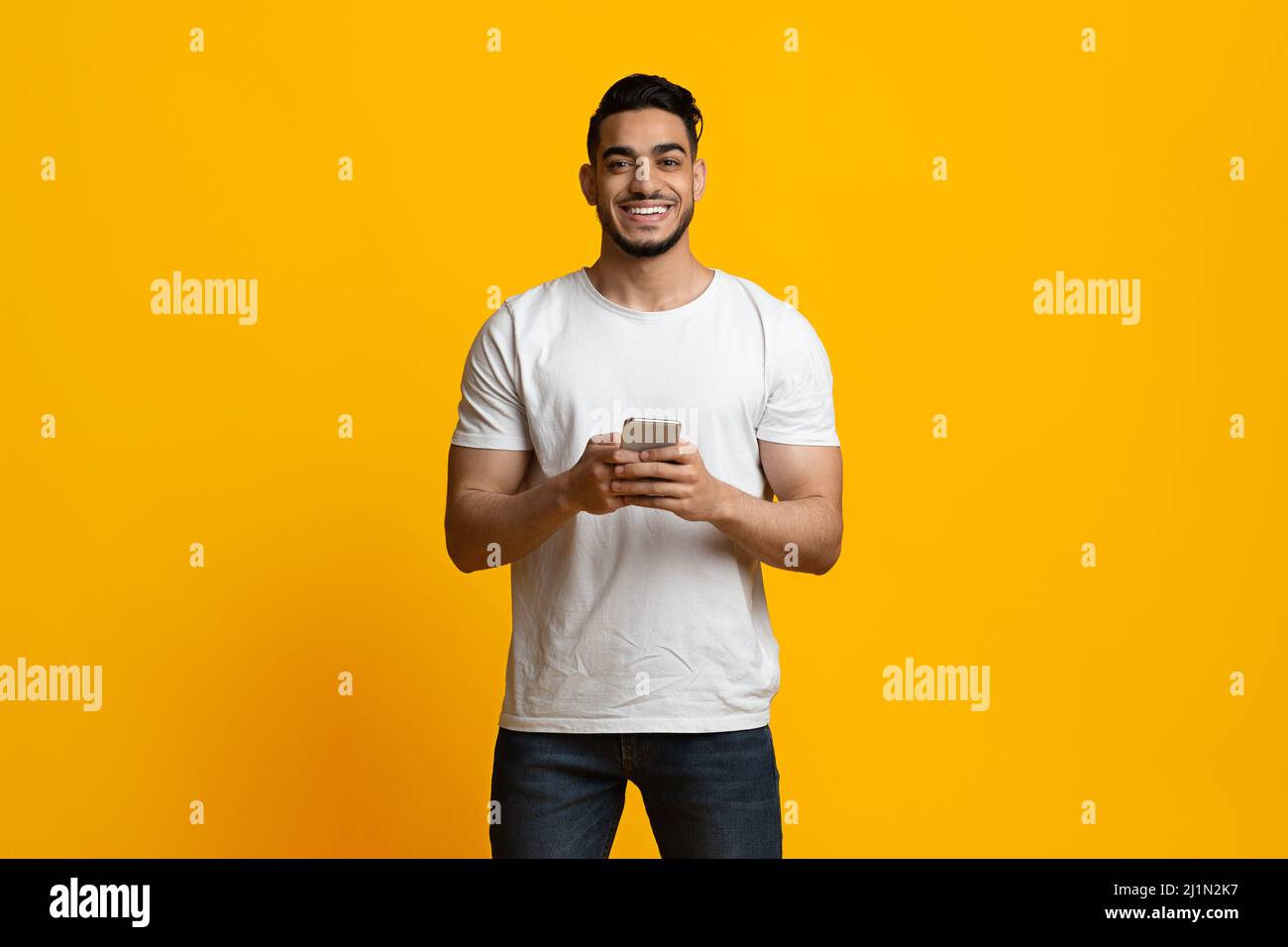 Cheerful arabic guy using mobile phone, yellow studio background Stock ...