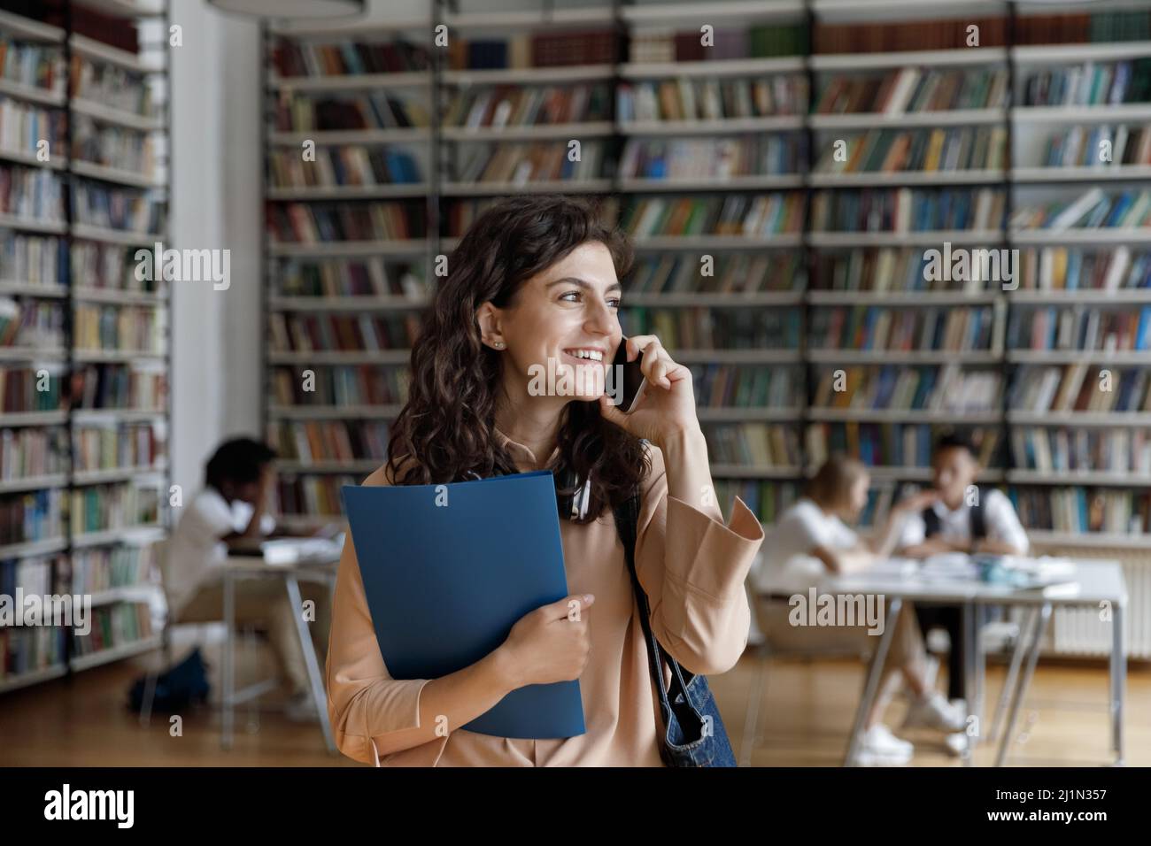 Attractive student girl standing in library talking on smartphone Stock ...