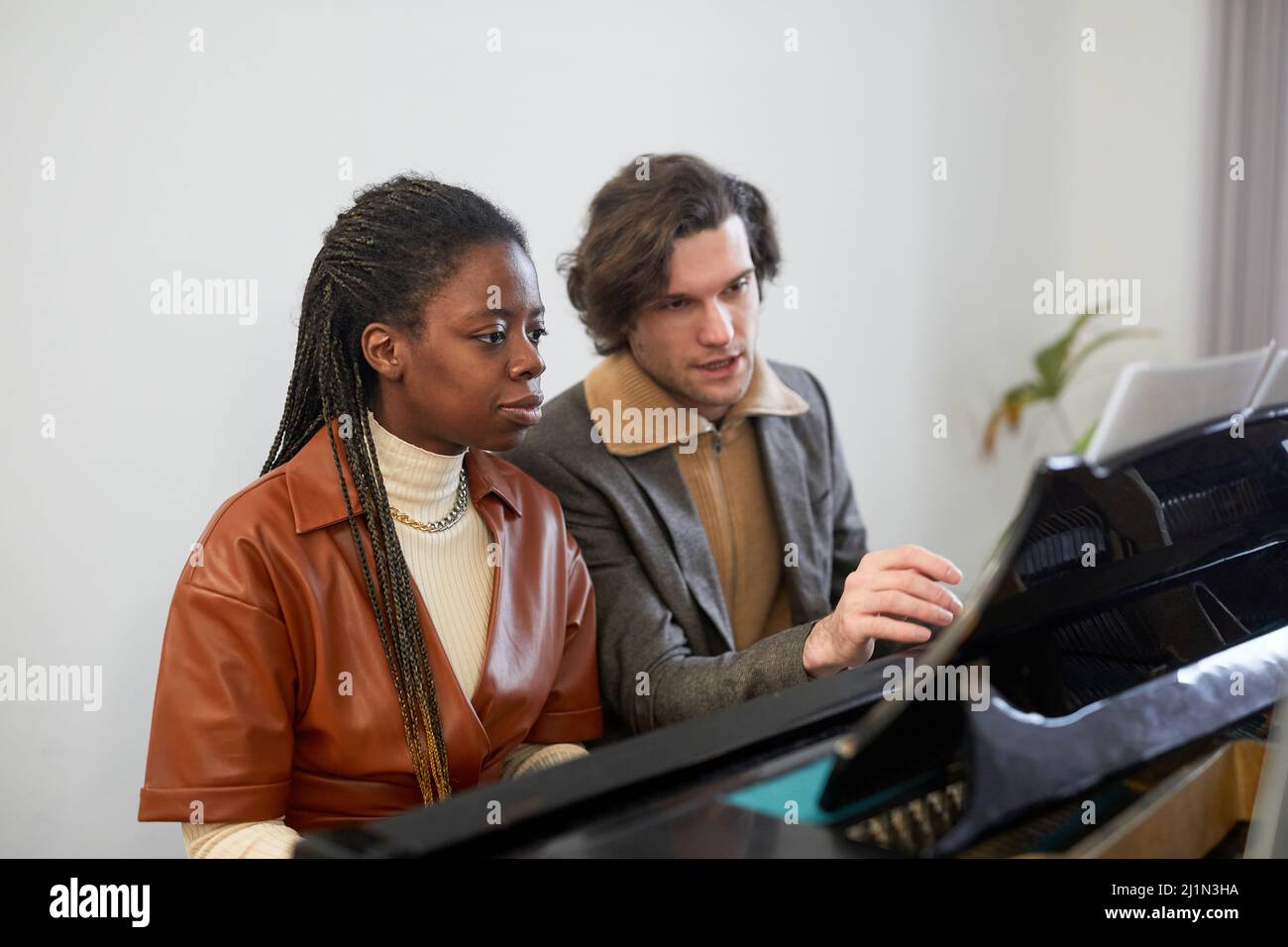 Young teacher pointing at sheet music and explaining to woman how to ...