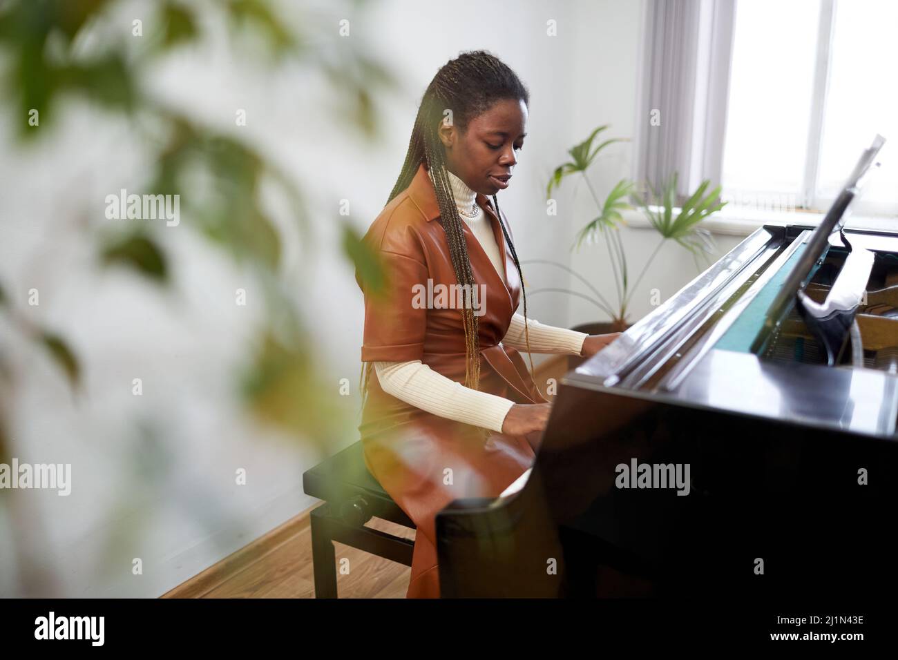African young woman sitting behind the grand piano and learning to play ...