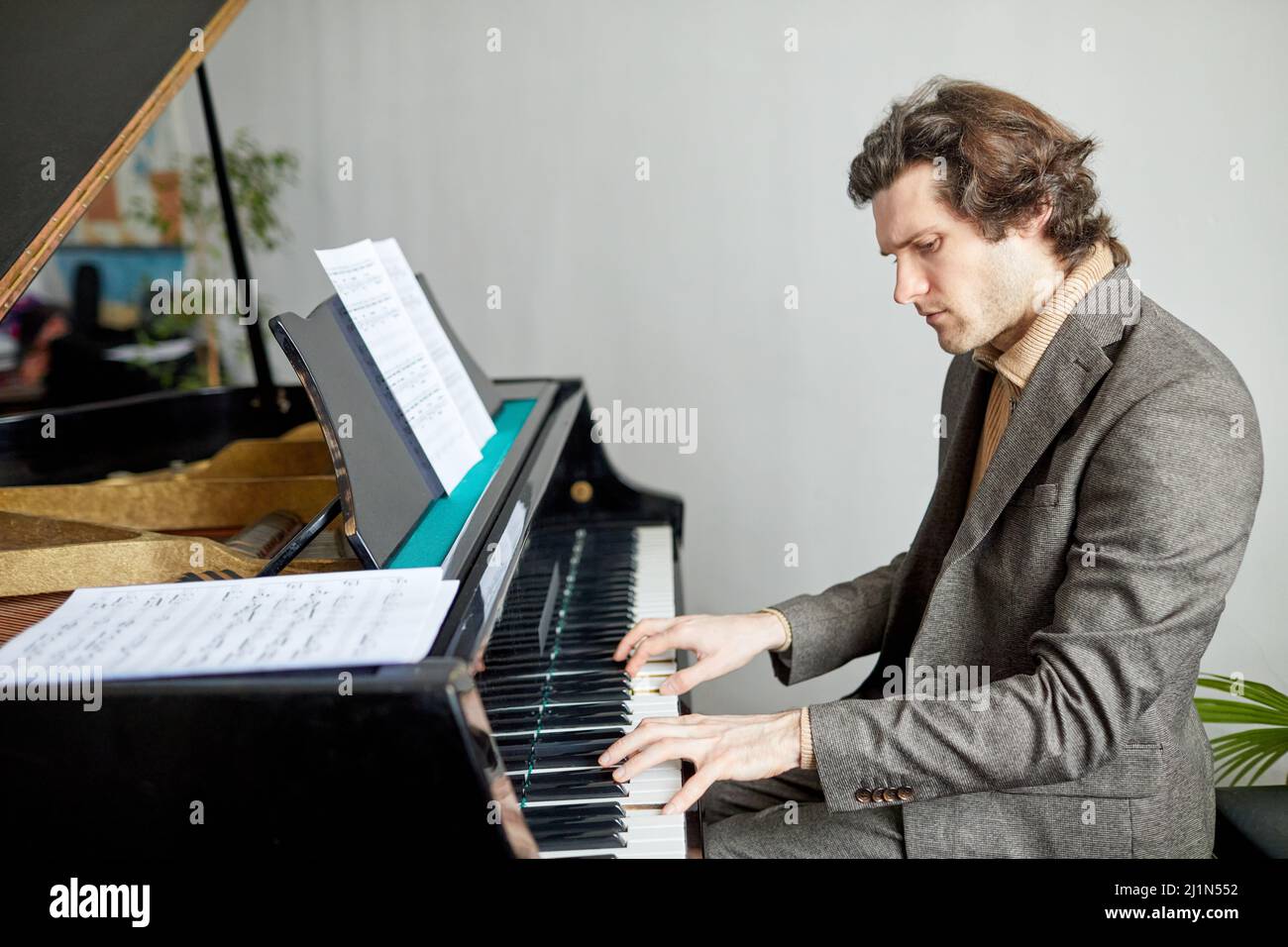 Serious pianist sitting at the piano in front of sheet music and ...