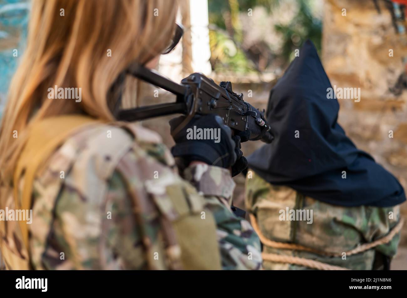 A caucasian woman in an army uniform holds a hostage with a bag on her ...