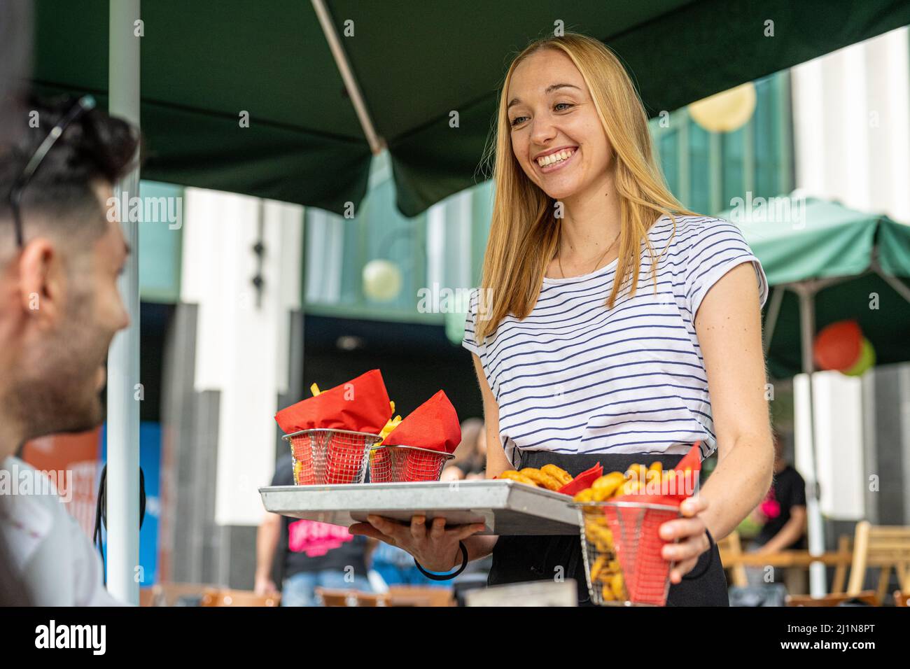 Young blonde waitress is serving French fries and beer to customers at ...
