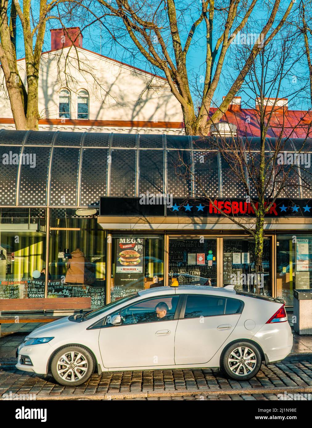 A vertical view of a white taxi in front of Hesburger in Tallinn ...