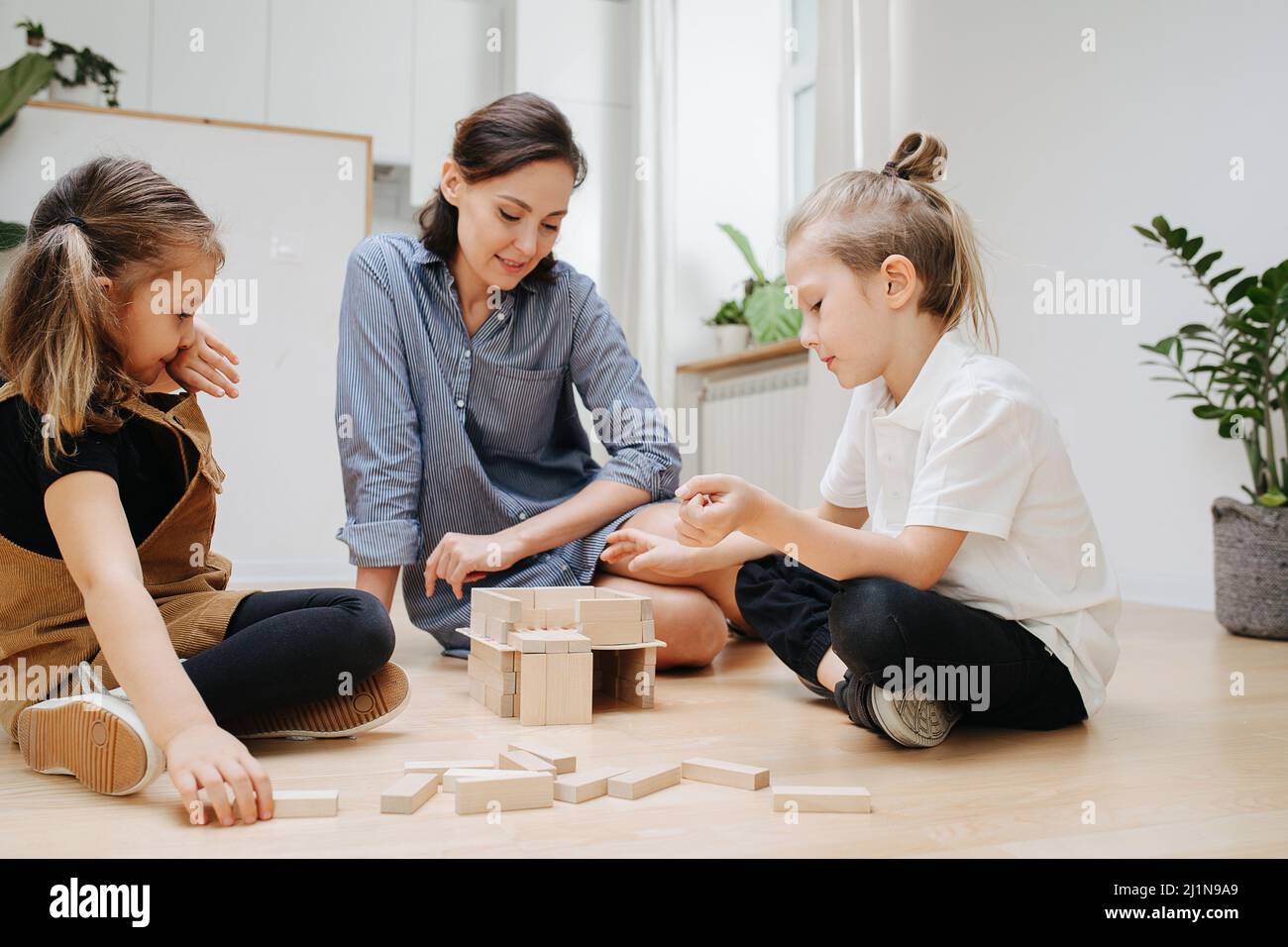 Cute family playing on the floor. Mom and two children. Building house ...